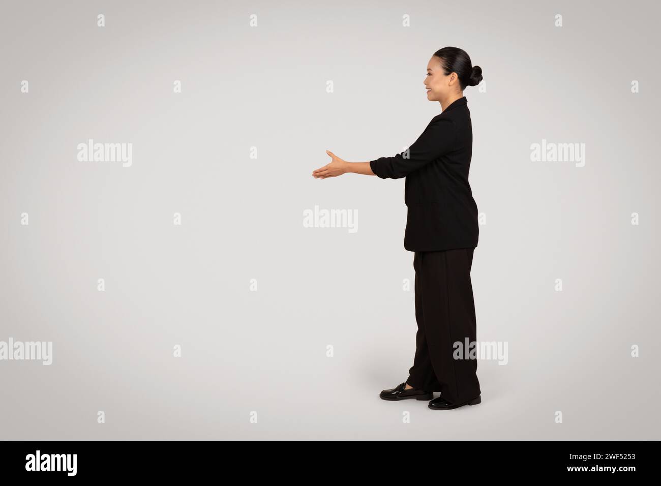Asian businesswoman in formal attire stands profile, extending a ...