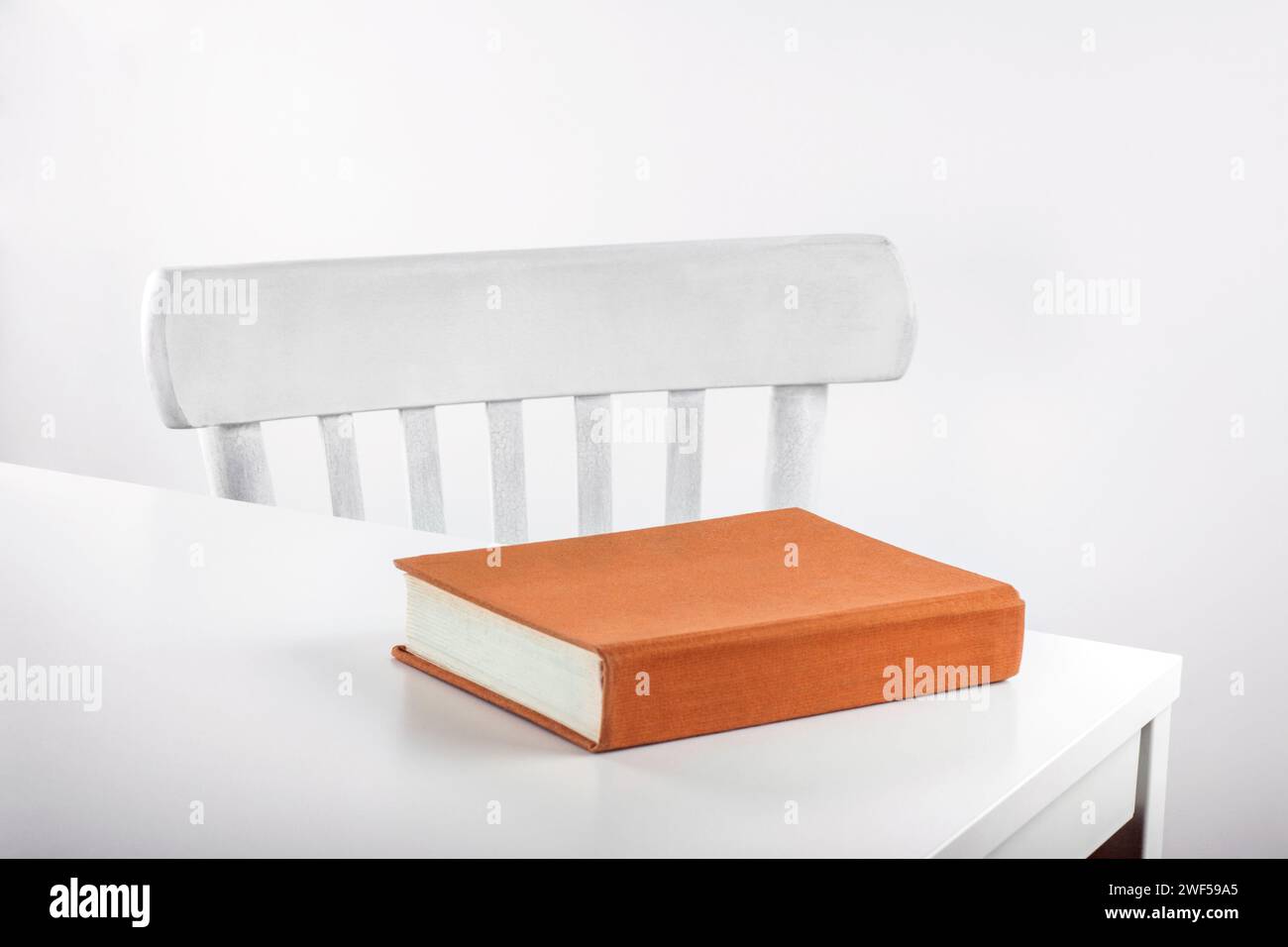 Closed book on a white table with a chair Stock Photo - Alamy