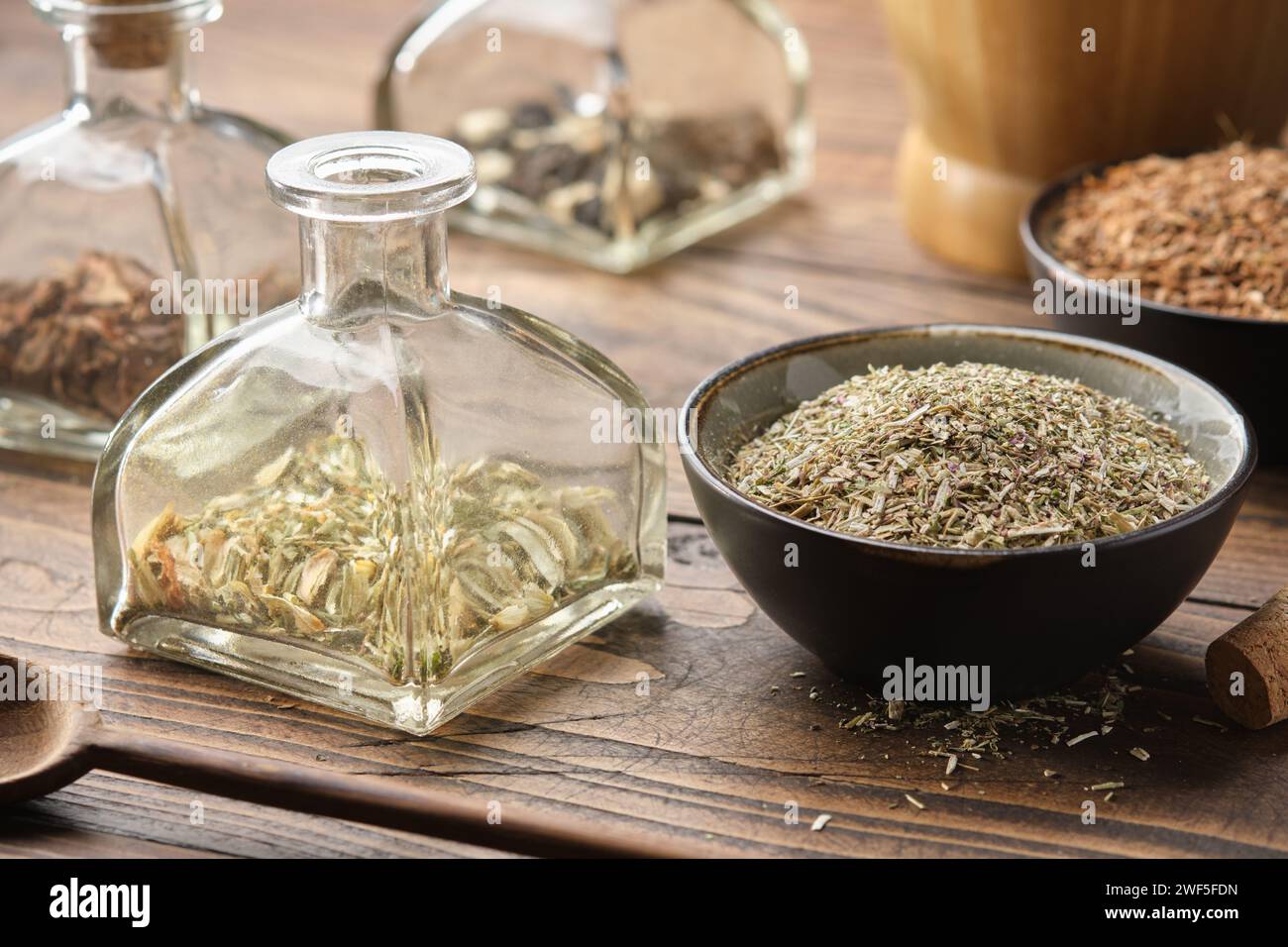 Bottle of dry herbs for making healing infusion or tincture. Bowls of ...