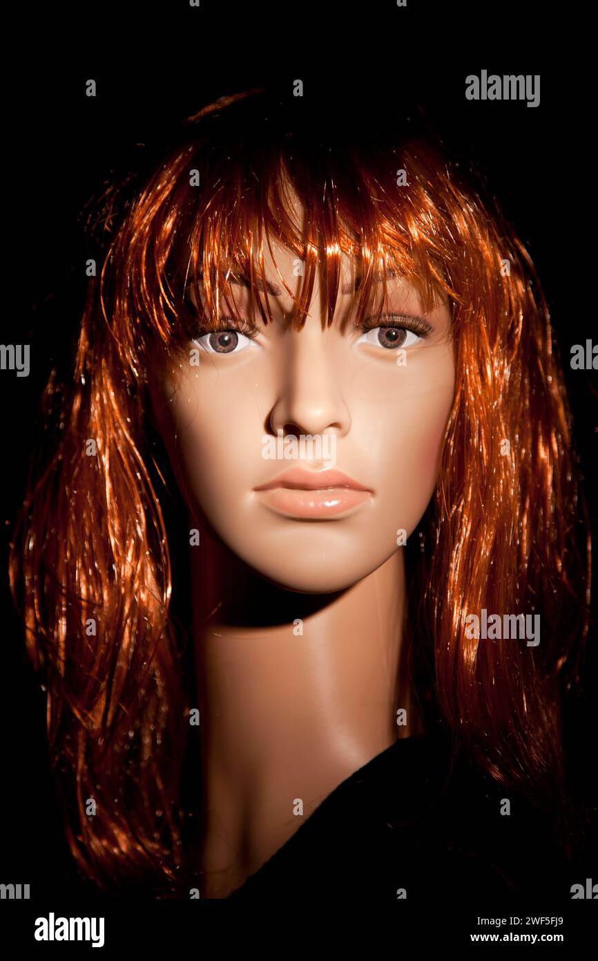 Red haired plastic woman mannequin with bright hair posing on a black ...