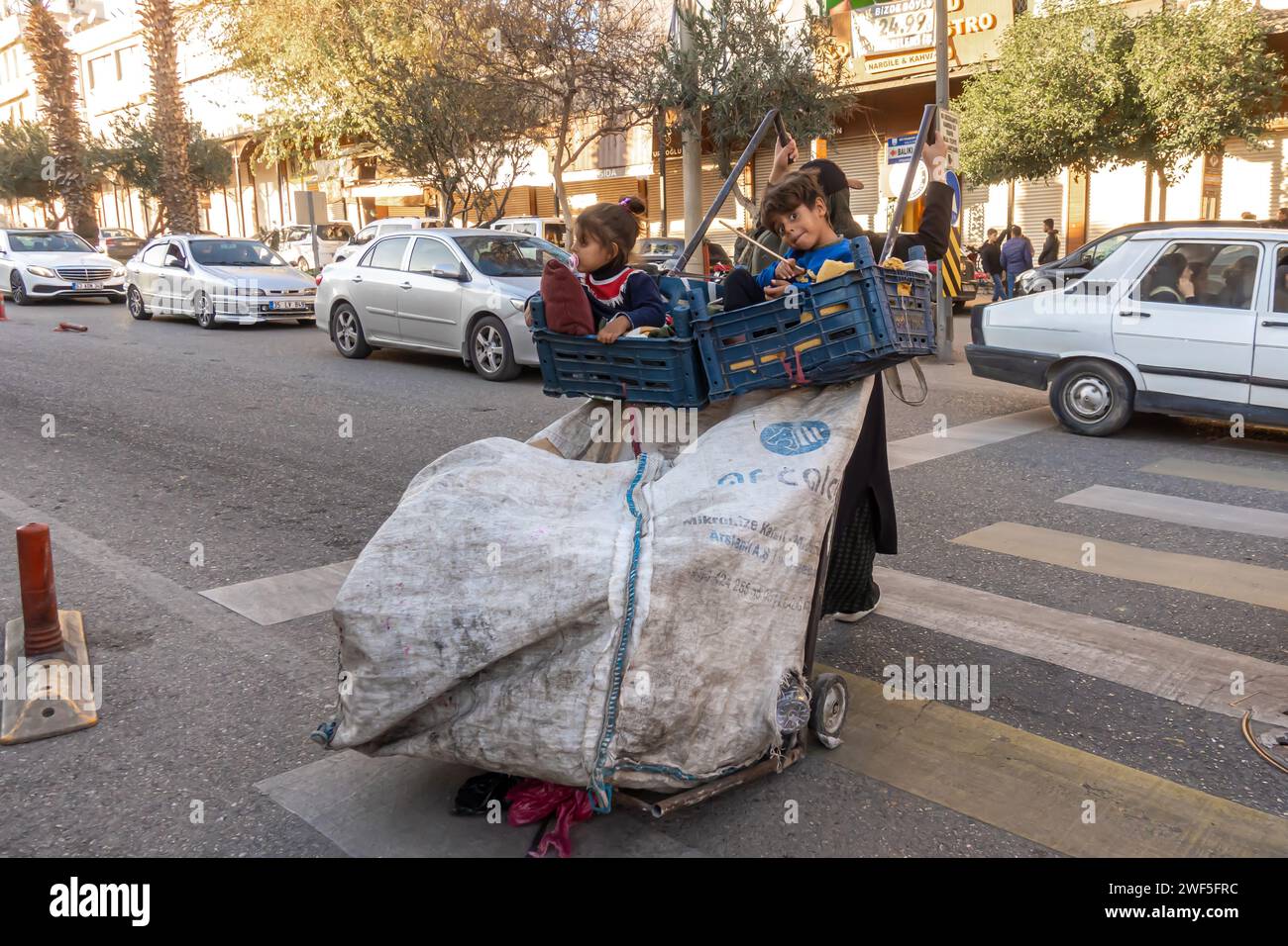 Middle Eastern refugees - a mother and babies using a grabage cart with ...