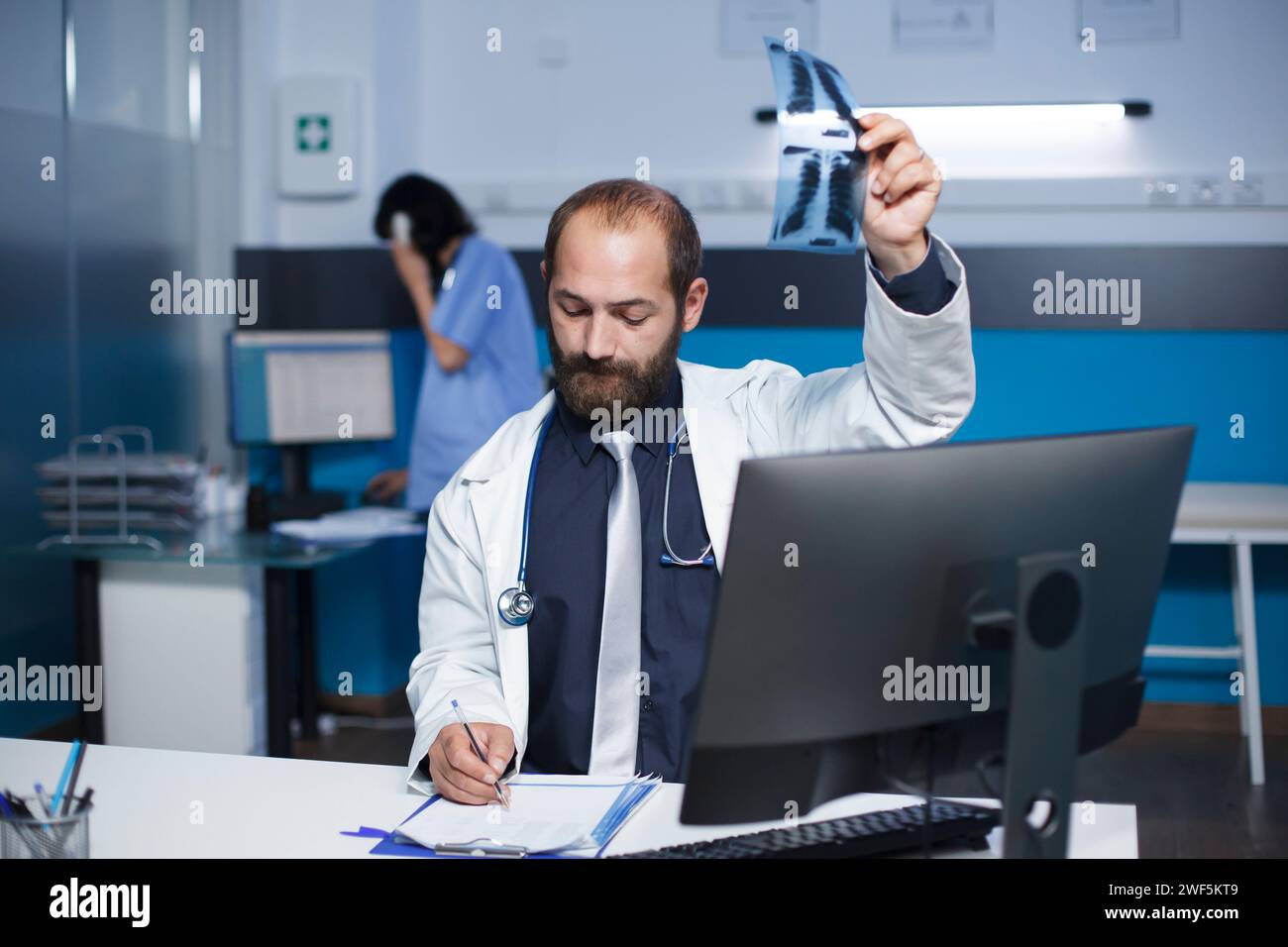 Young physician grasping an X-ray image and writing notes on his ...