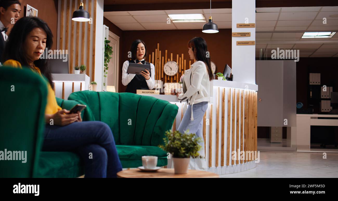 Asian guest signing check in papers on tablet at reception, registering ...