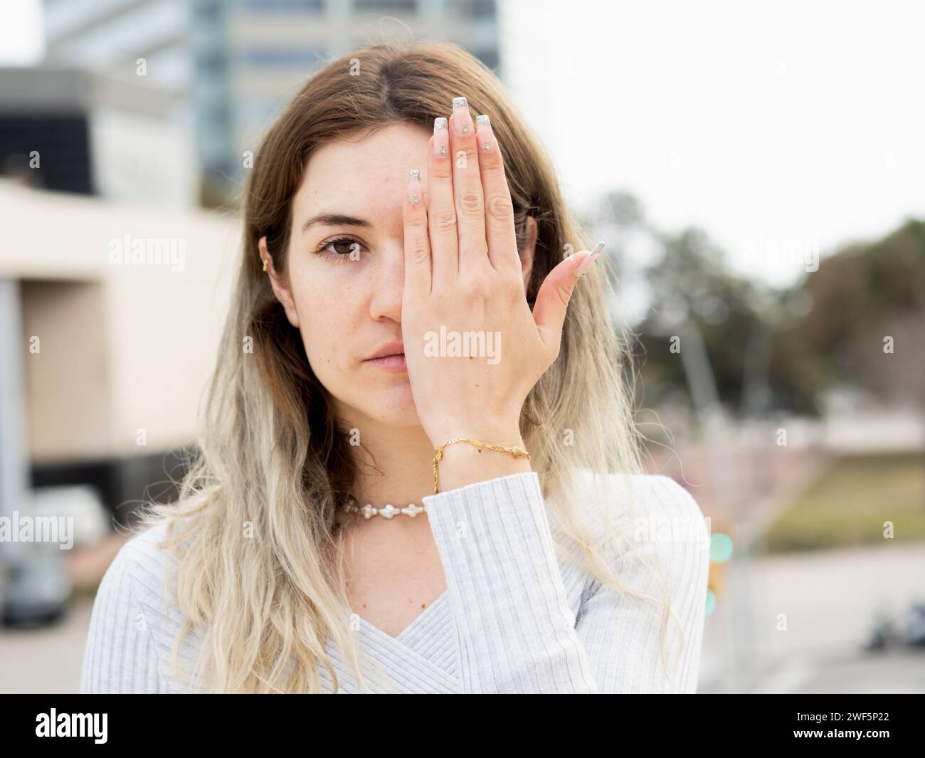 Portrait of a young blonde woman covering one eye with her hand looking ...