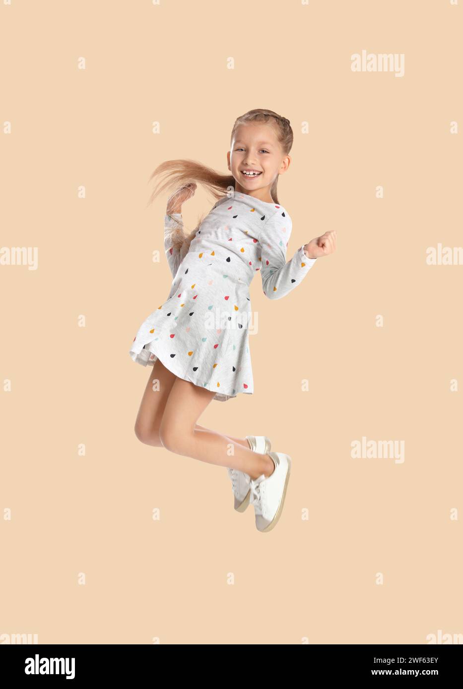 Happy cute girl jumping on beige background Stock Photo - Alamy