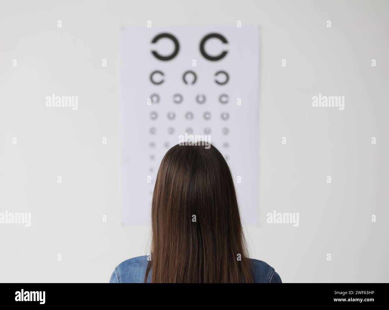 Eyesight examination. Young woman looking at vision test chart indoors ...