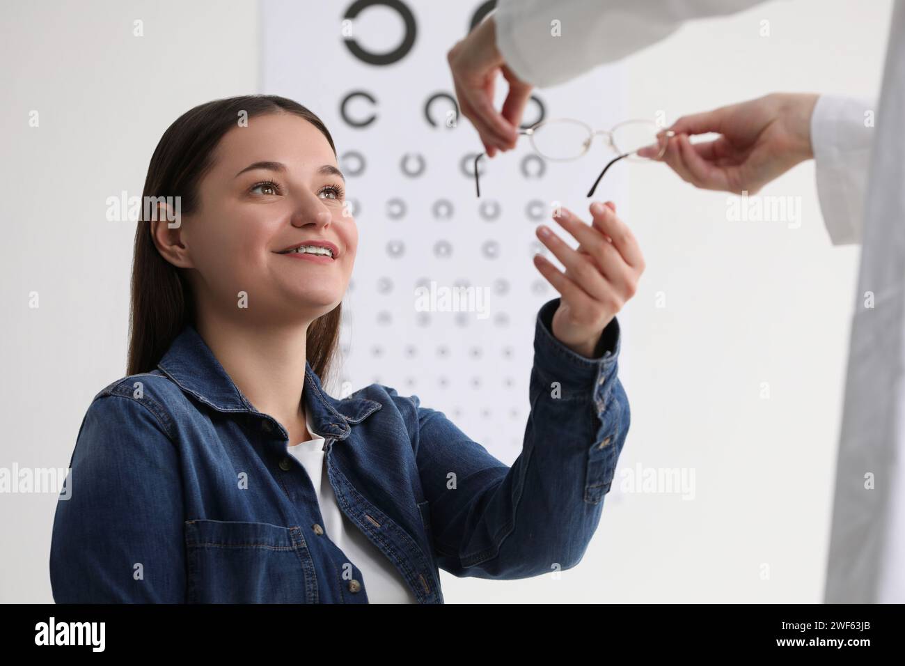 Vision testing. Ophthalmologist giving glasses to young woman indoors ...