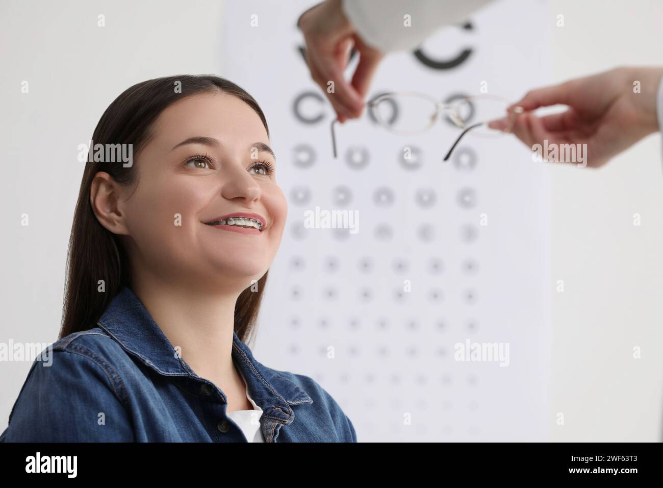 Vision testing. Ophthalmologist giving glasses to young woman indoors ...