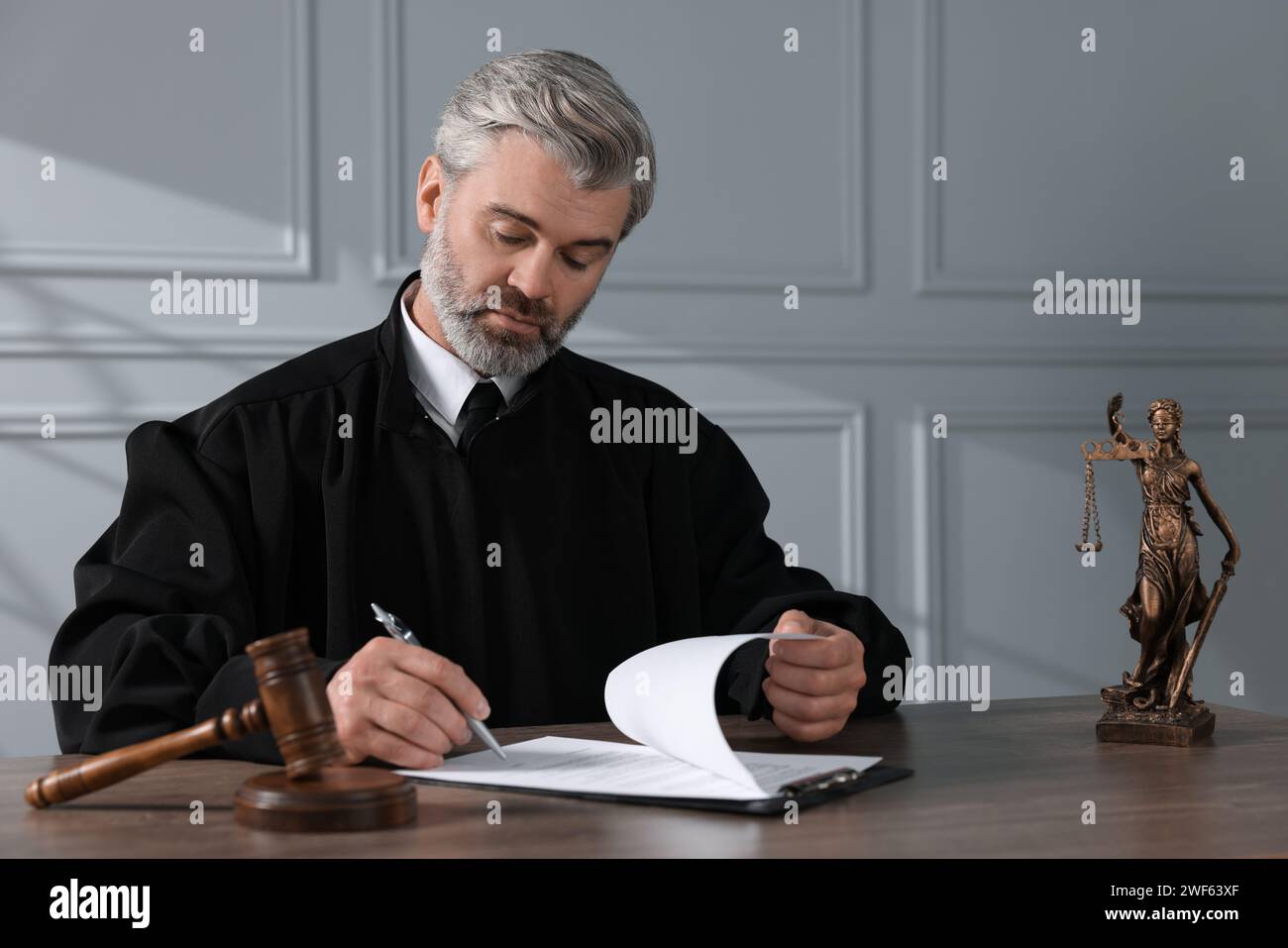 Judge with gavel writing in papers at wooden table indoors Stock Photo ...