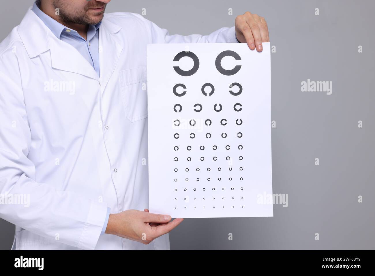 Ophthalmologist with vision test chart on gray background, closeup ...