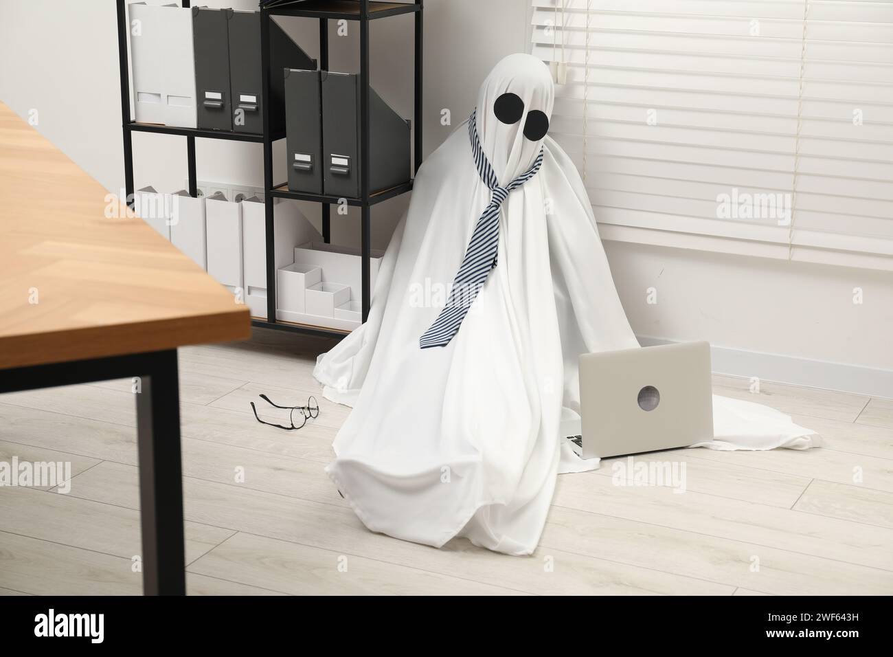 Overworked ghost. Man in white sheet with laptop on floor in office ...