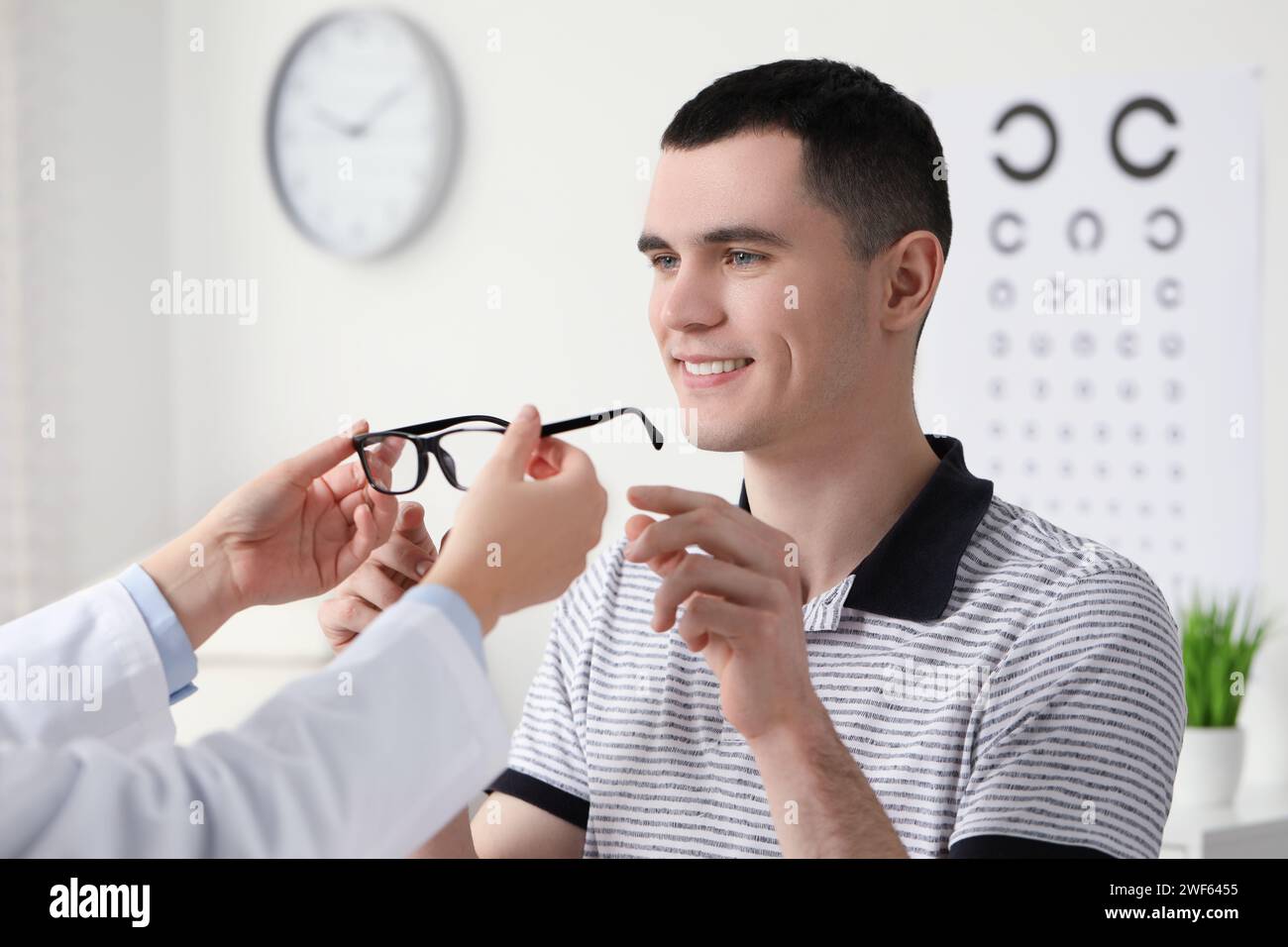 Vision testing. Ophthalmologist giving glasses to young man indoors ...