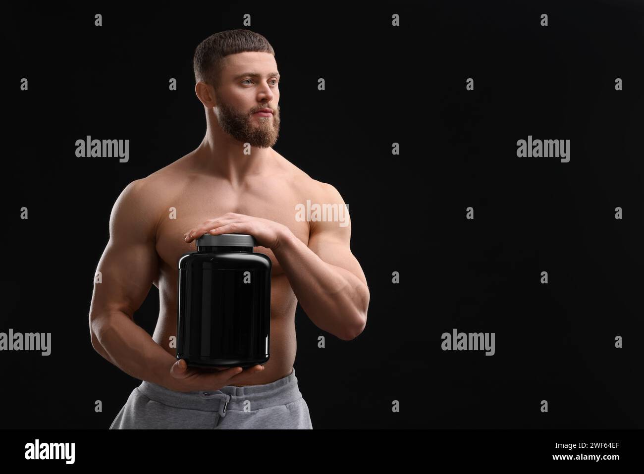 Young man with muscular body holding jar of protein powder on black ...