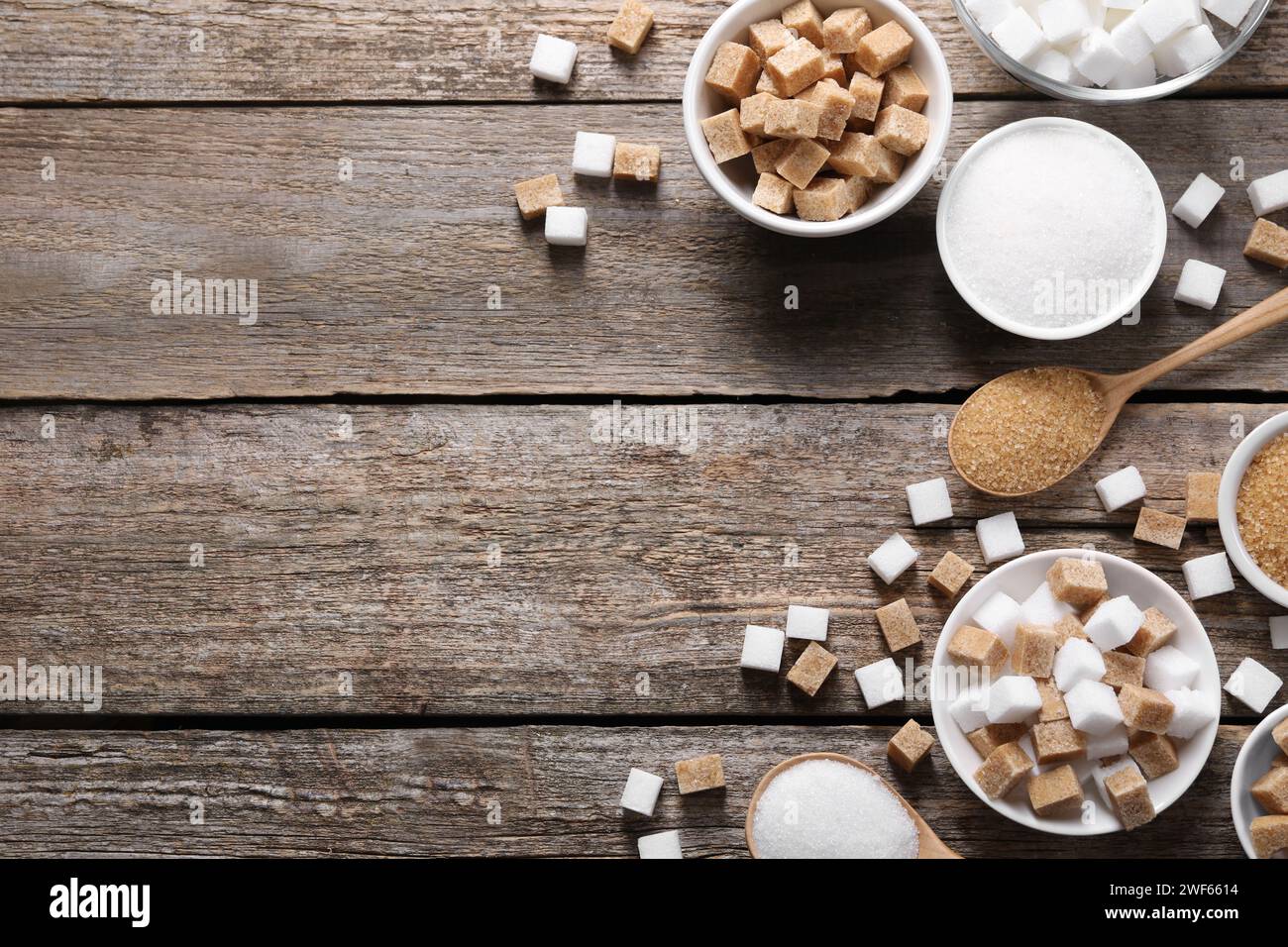 Different types of sugar in bowls and spoons on wooden table, flat lay ...