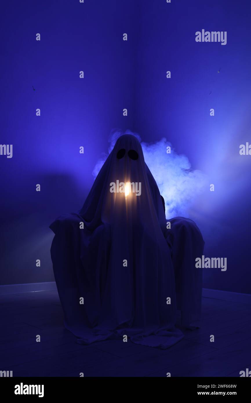 Creepy ghost. Woman covered with sheet in armchair in blue light Stock ...