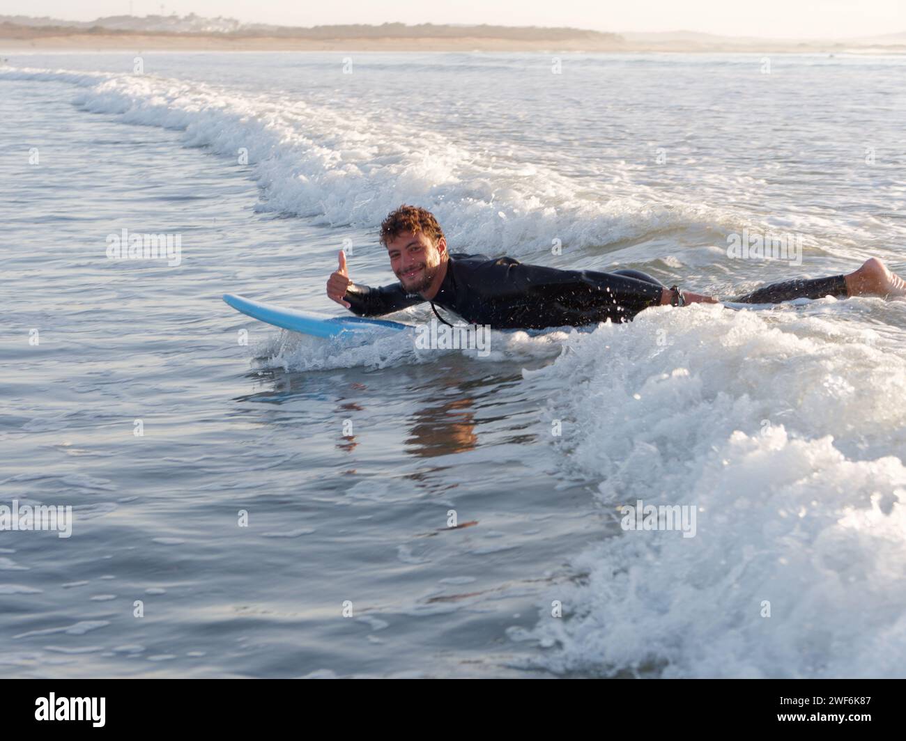 Surfer flat on his board in shallow water smailing and giving a thumbs ...