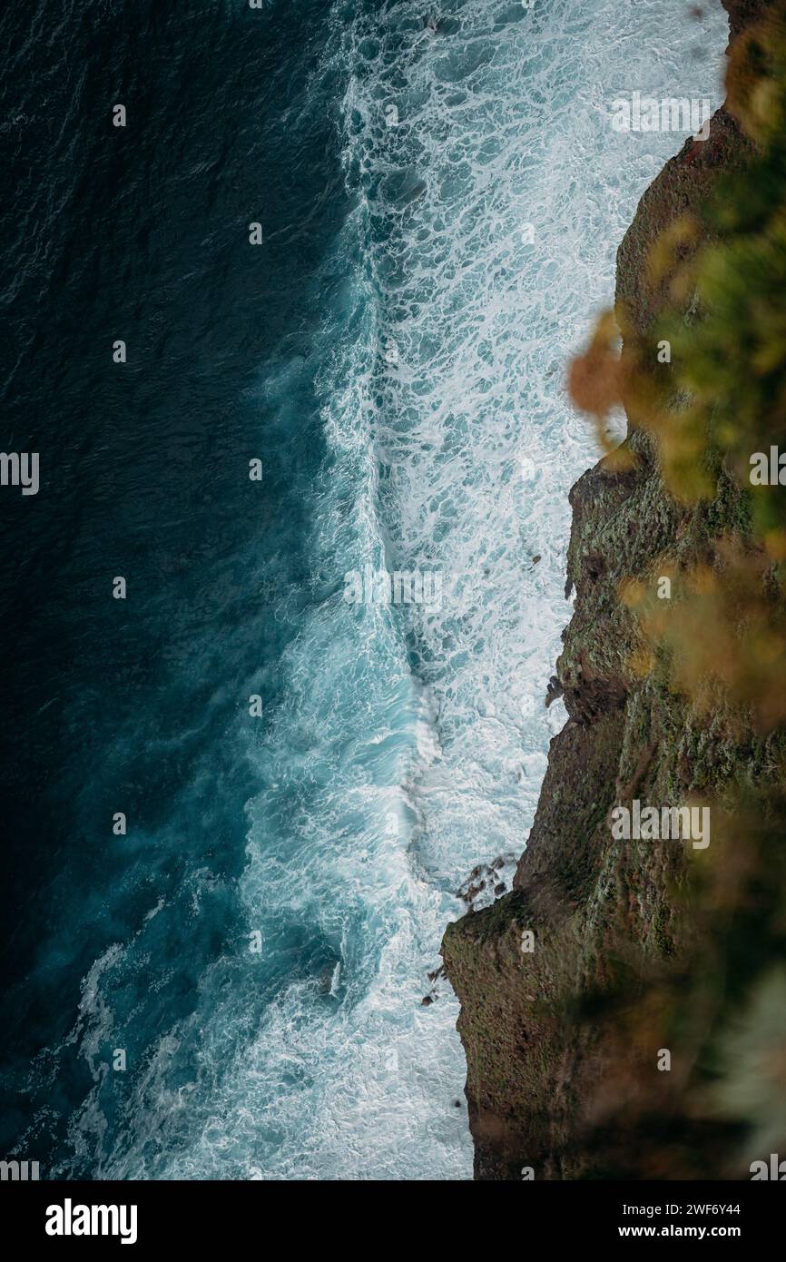 An aerial view of turbulent sea waves crashing against rocky shore ...