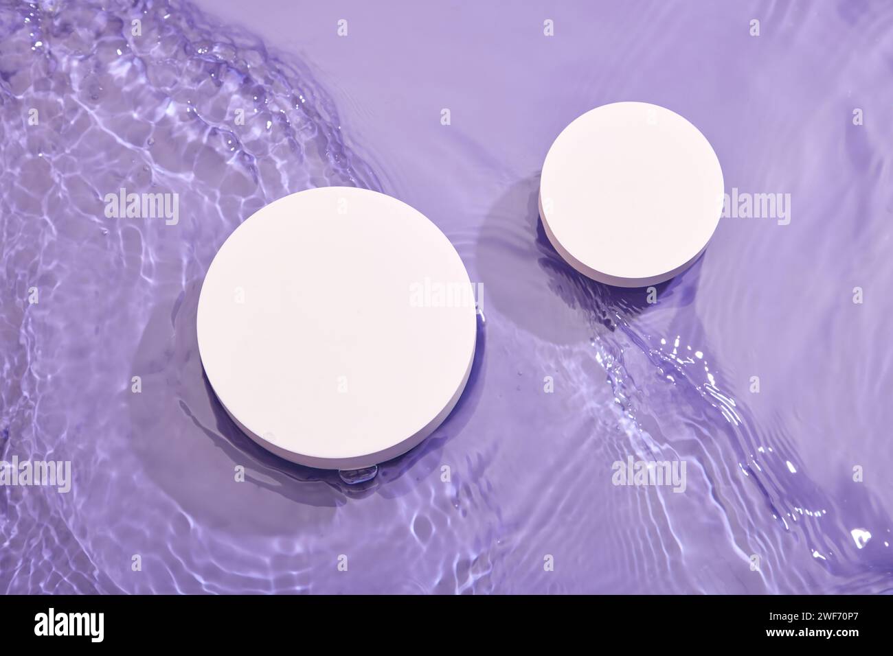 Two white circular empty podiums, set on a purple background with water ...