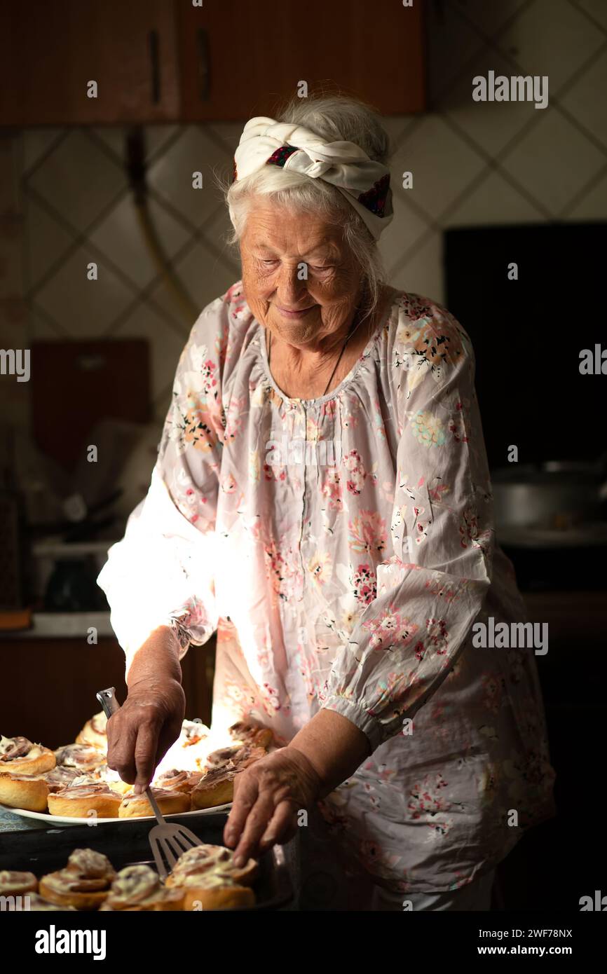 happy old woman Granny cooks in kitchen cinnamon rolls and bakes ...