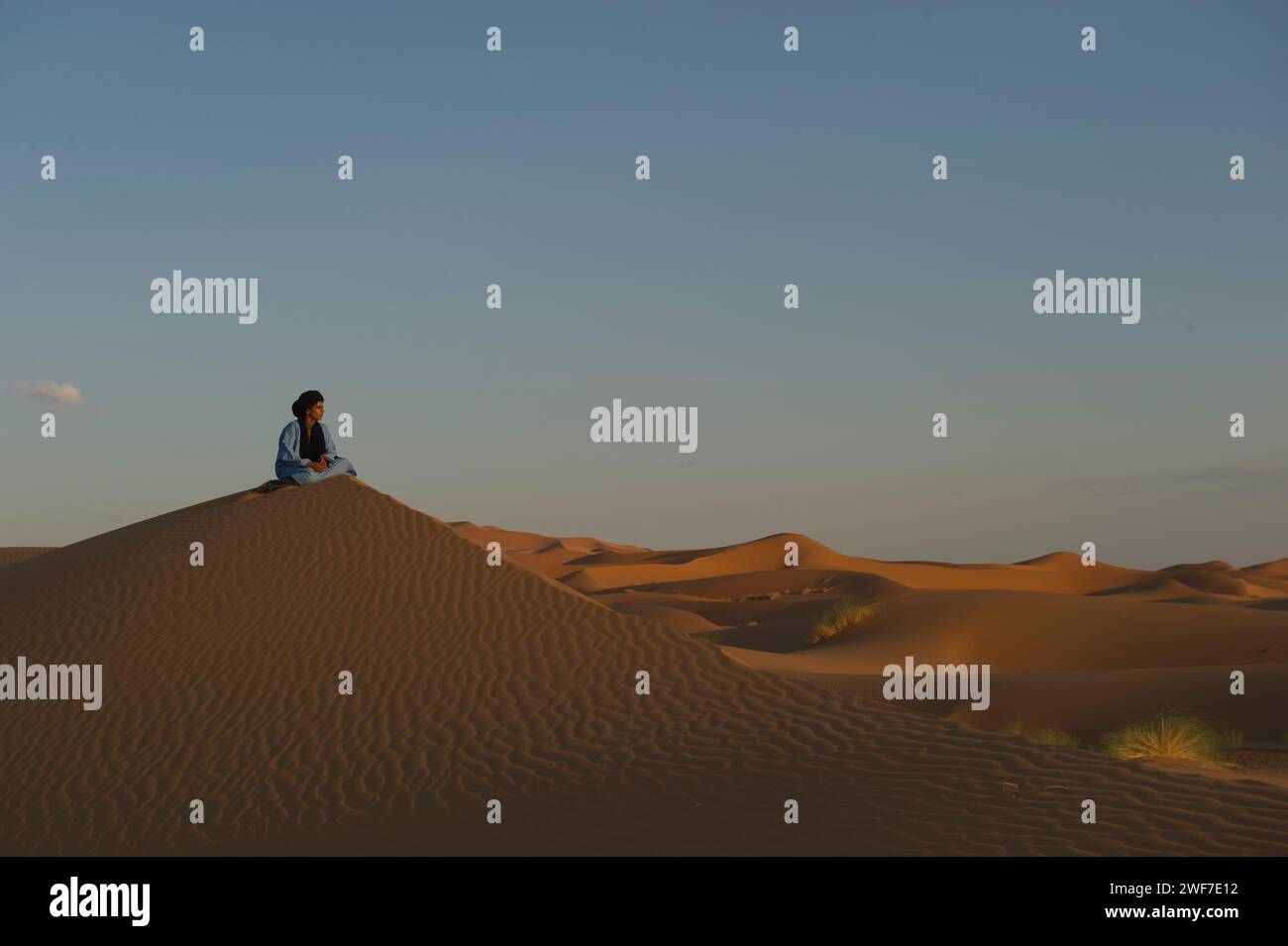 A desert guide in traditional dress sits on a dune at sunset Stock ...