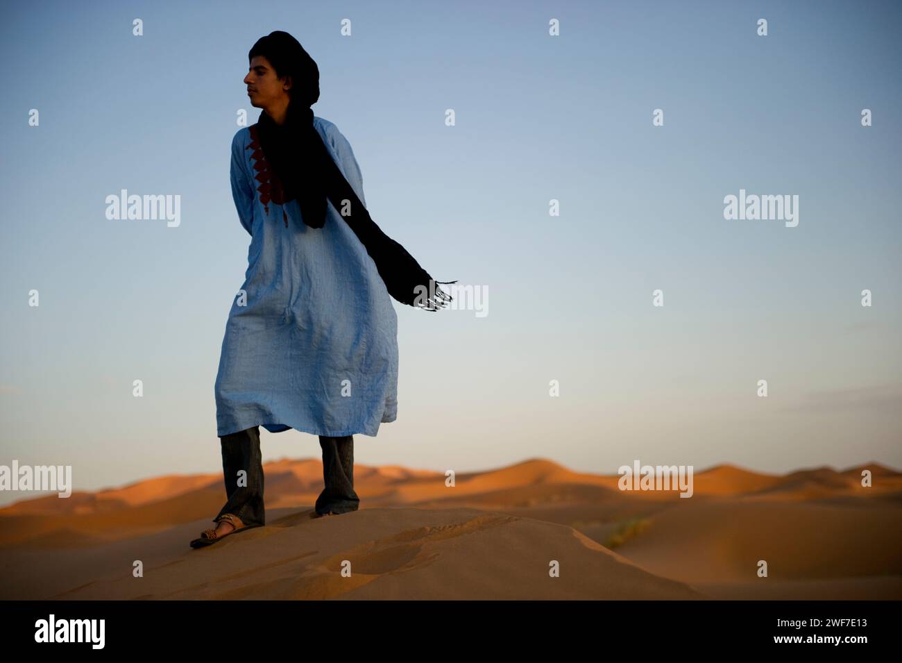 A desert guide in traditional dress stands on a dune at sunset Stock ...