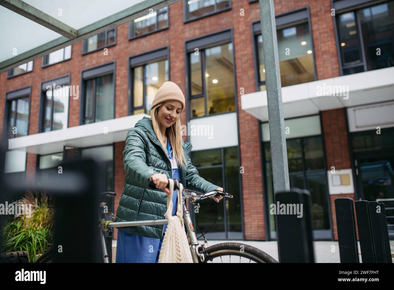 Beautiful nurse commuting through the city by bike. Doctor city leaving hospital by bike after ...