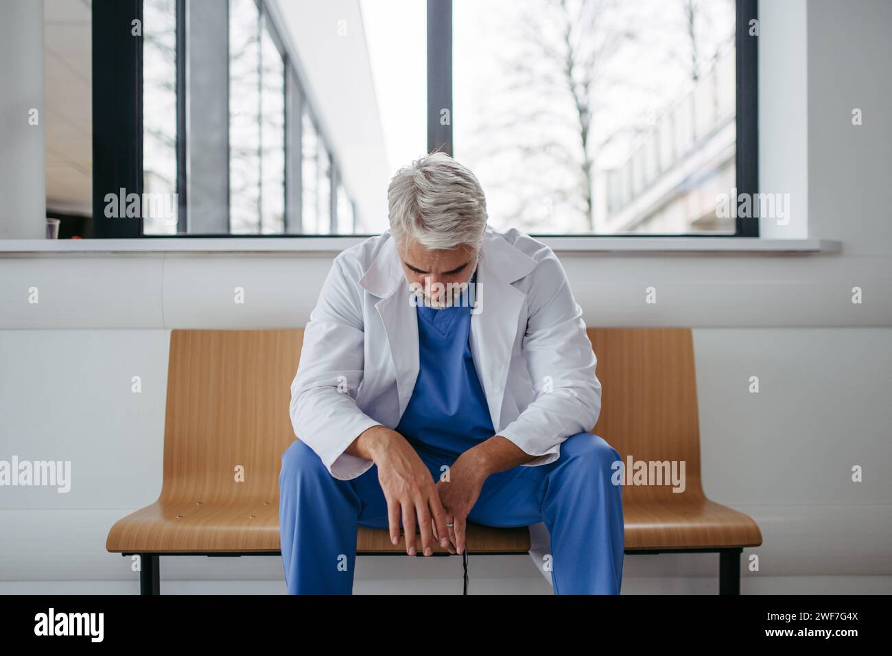 Frustrated, exhausted doctor sitting on bench in hospital corridor ...