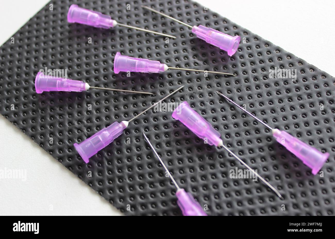 Open needles for disposable syringes are scattered on a black medical ...