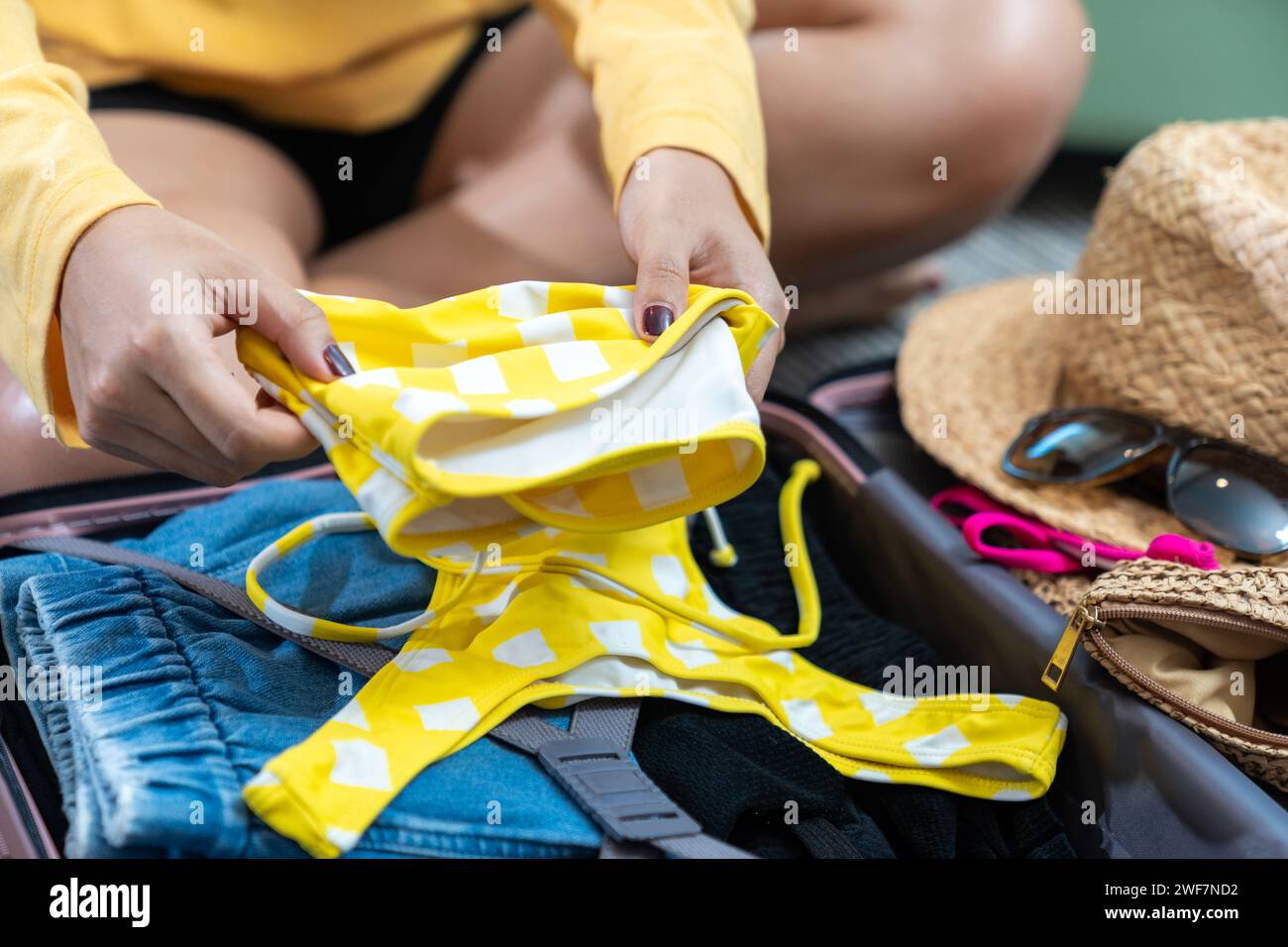 A young woman preparing to pack her bikini into her travel bag for a ...