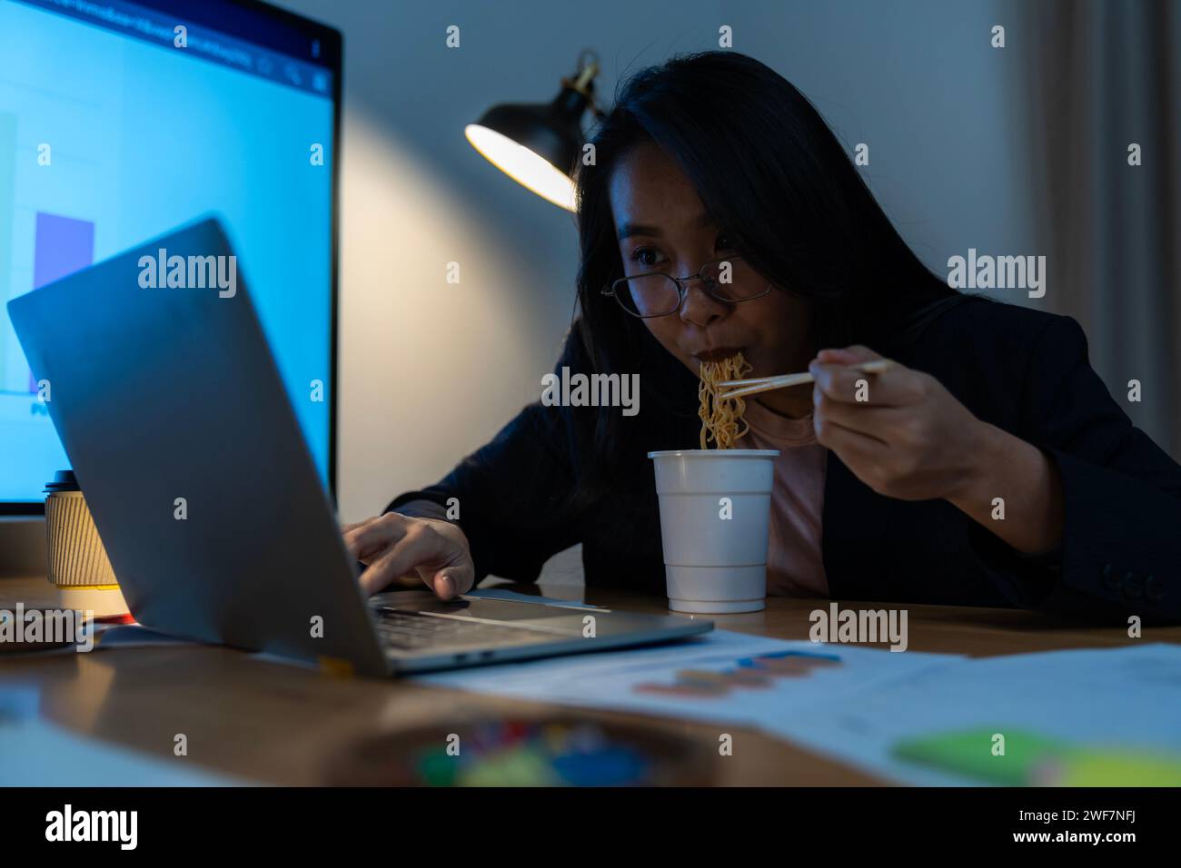 A female office worker working late and eating instant noodles alone in ...