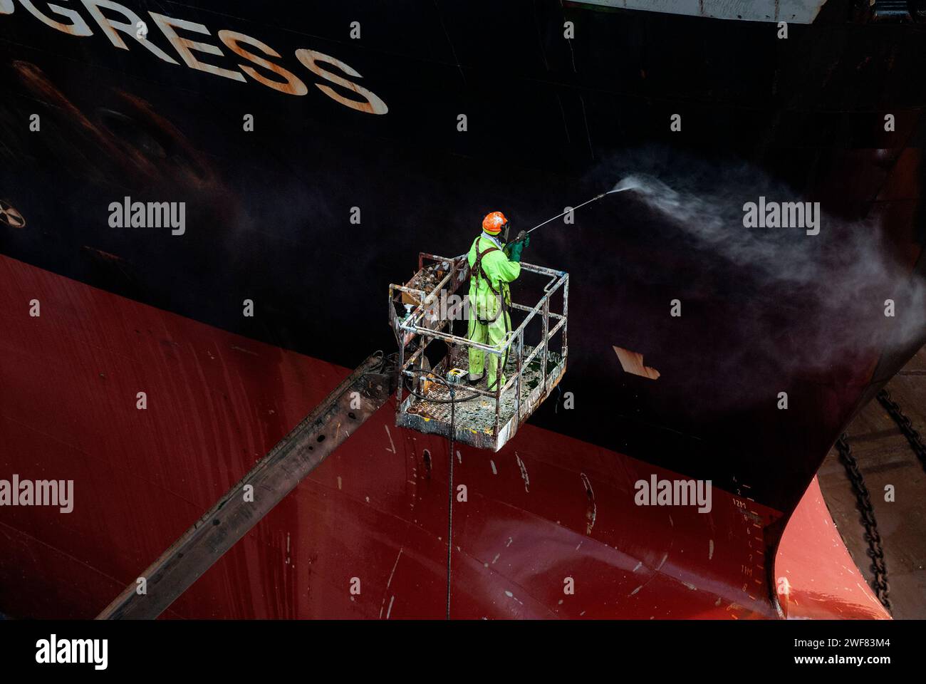 High angle image of a dock worker steam cleaning the hull of a tanker ...