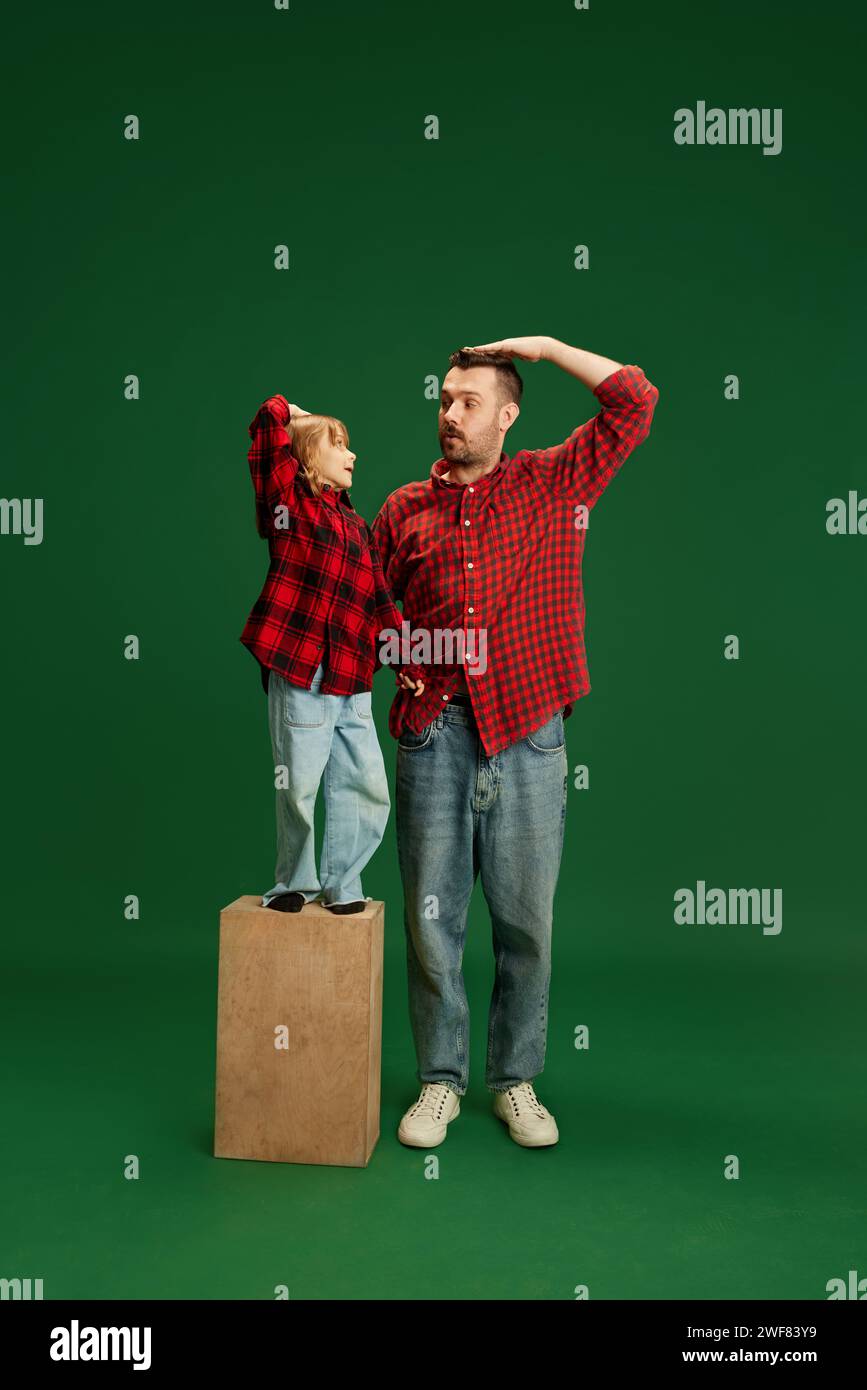 Child on pedestal and father standing beside, both posing with hands on ...