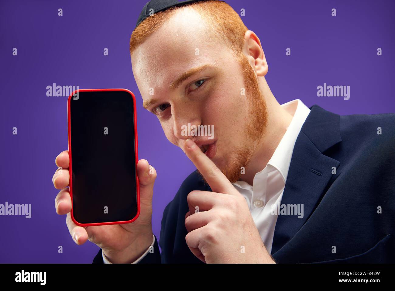 Young Jewish emotional ma showing mobile phone screen against purple ...