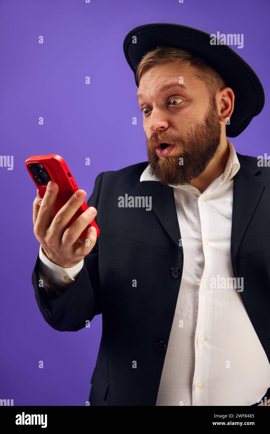 Bearded young Jewish man emotionally looking on mobile phone screen ...