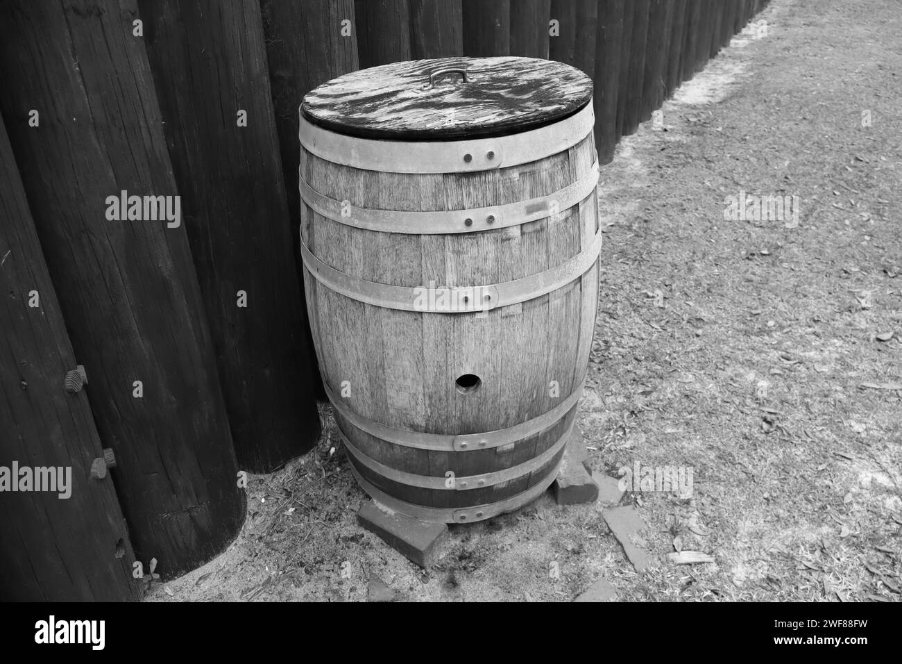 A black and white shot of a barrel placed adjacent to a rustic wooden ...