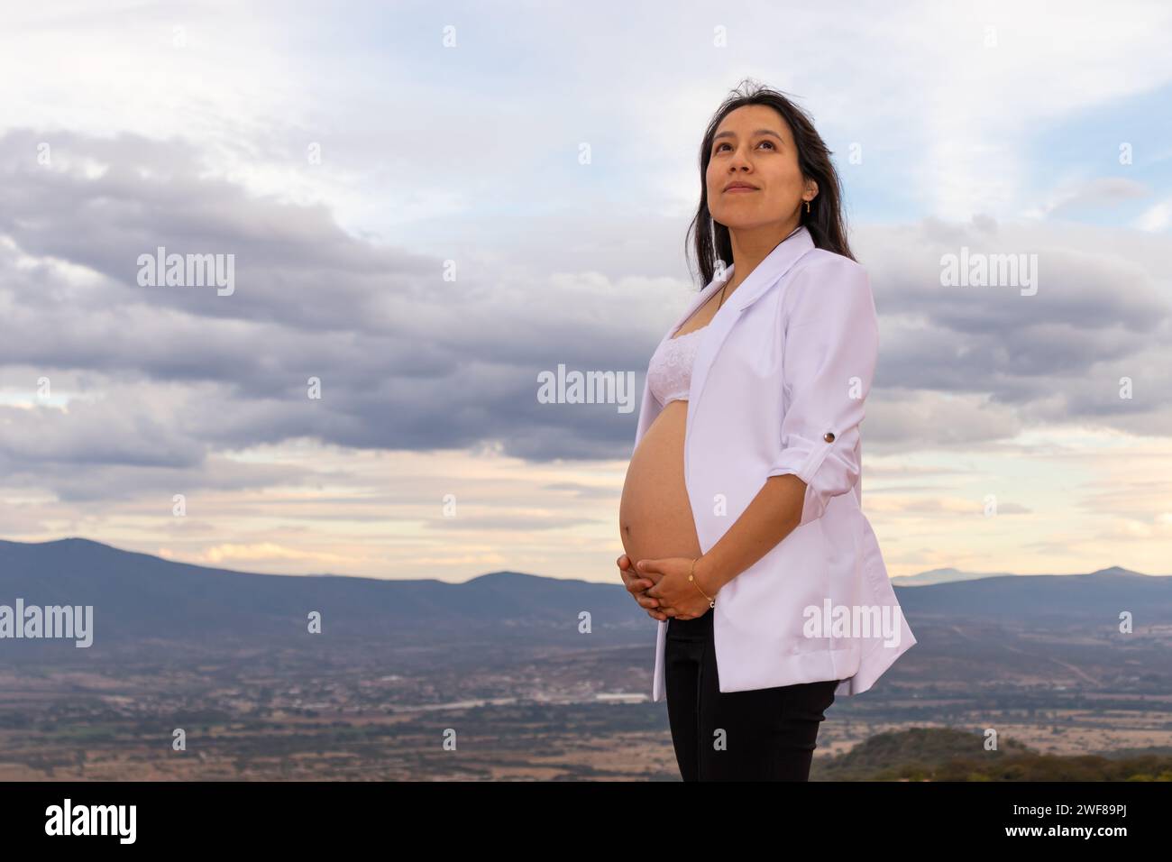 From below of contemplative pregnant woman cradles her belly against a ...