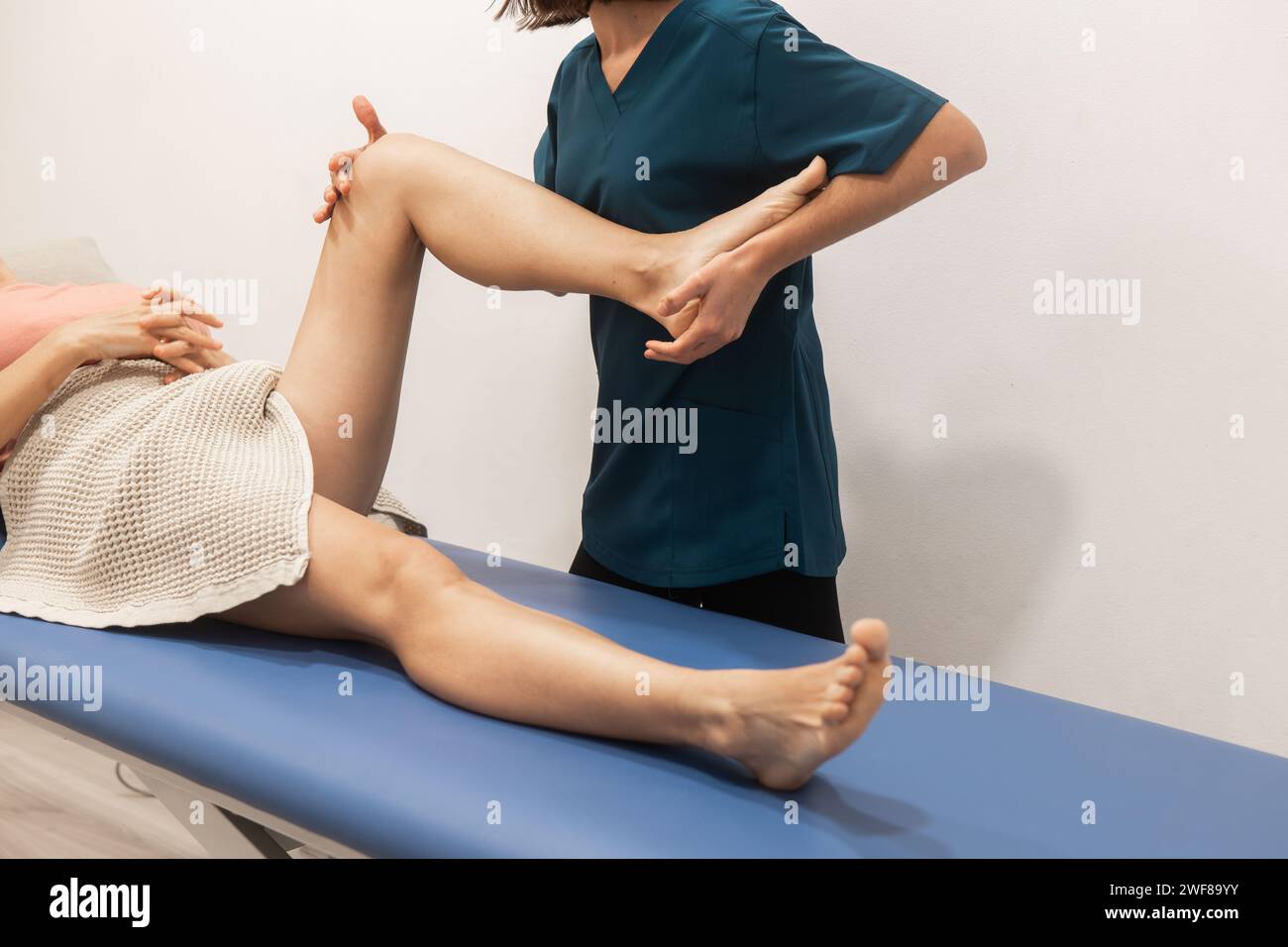 Female physiotherapist assessing a patient's leg function during a ...