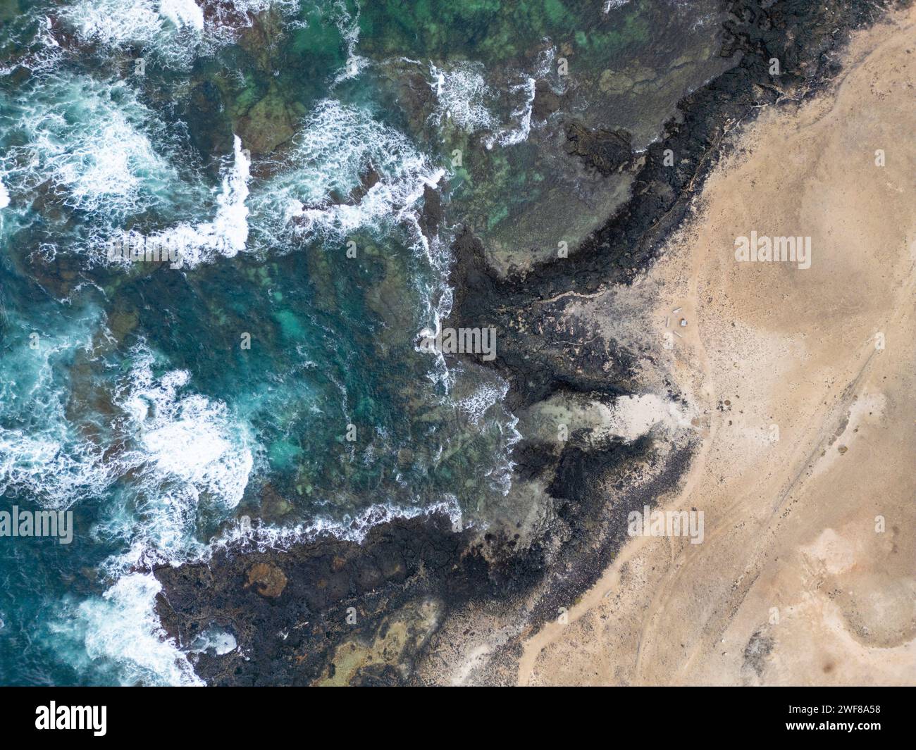 Aerial view of frothy waves lapping against the rocky shores and sandy ...