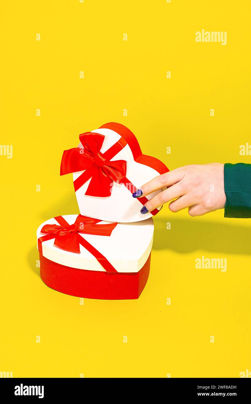 Anonymous hand touching the lid of a heart-shaped gift box with a red ...