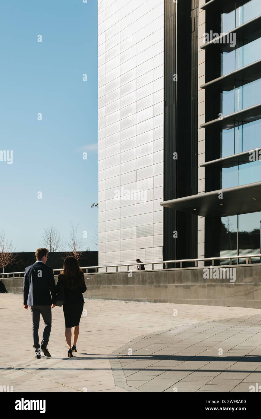 A couple walks hand in hand past a sleek building, embodying urban ...
