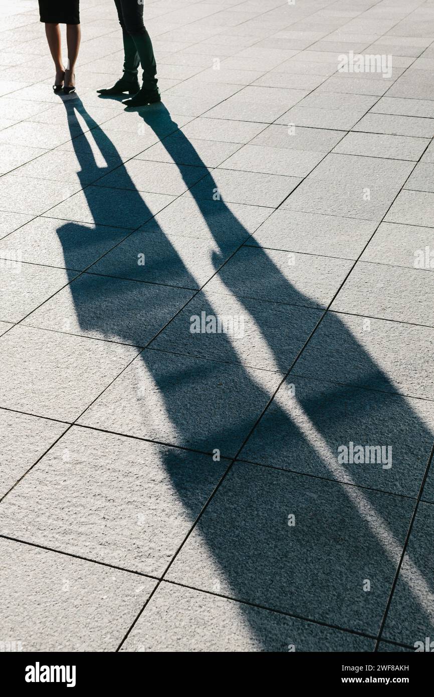 The image captures the elongated shadows of two individuals cast on the smooth pavement ...