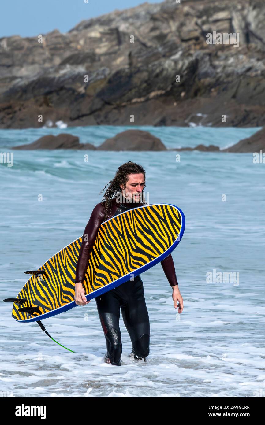 A surfer carrying his distinctive surfboard after a surfing session at ...