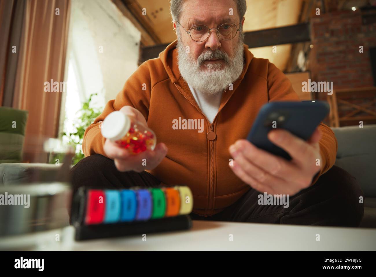 Elderly man examining pill bottle while looking at smartphone. Using ...
