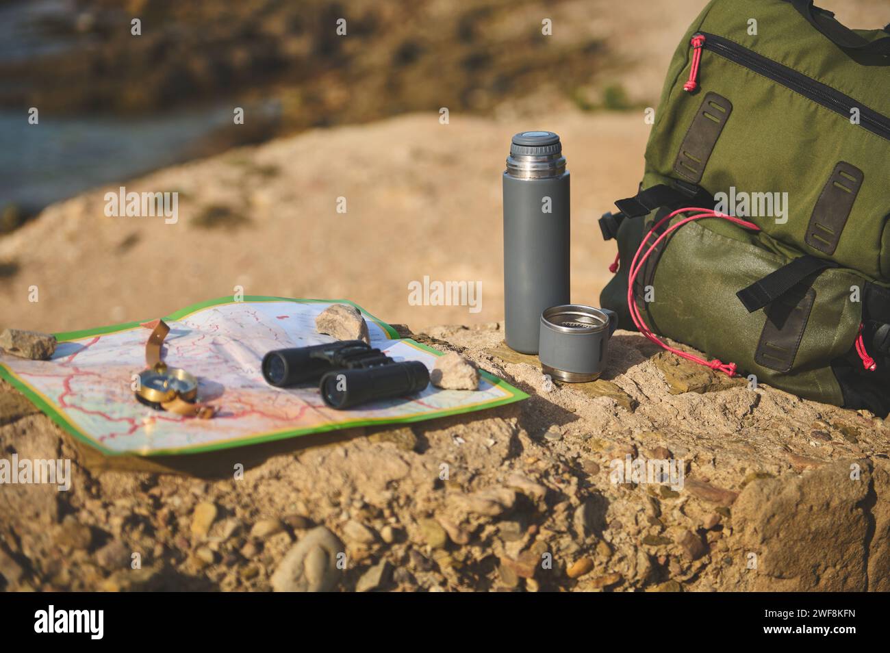 Still life with a green backpack nd thermos flask on the cliff against ...