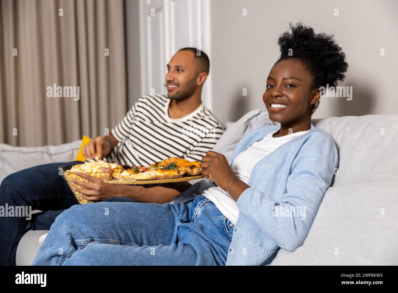 Couple eating pizza and popcorn watching comedy film sitting on couch ...