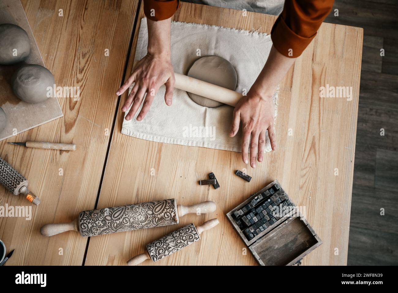 Artisan woman in lighted pottery studio, rolling clay for modelling ...