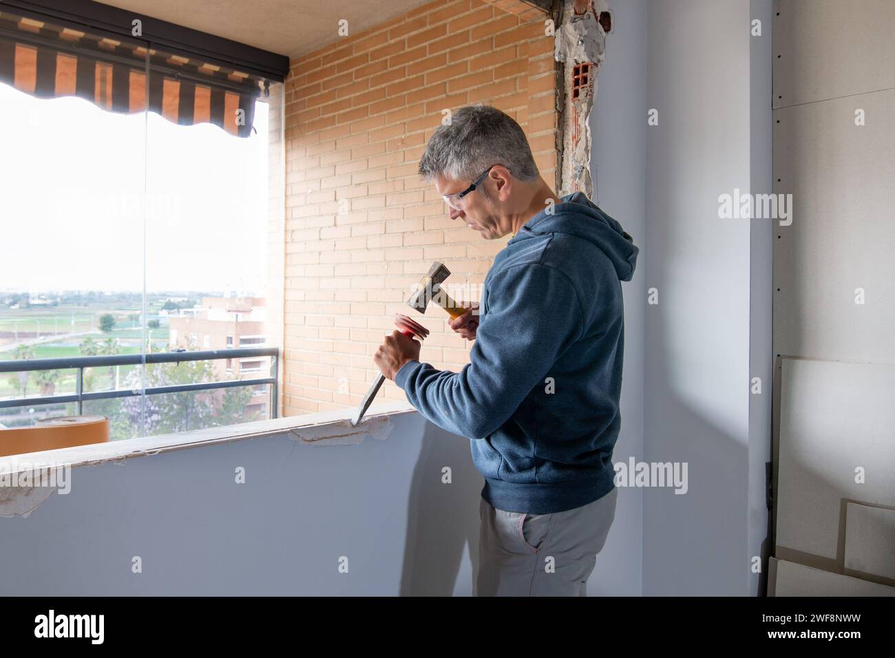 A bricklayer works on installing a new window in a home, chipping walls ...