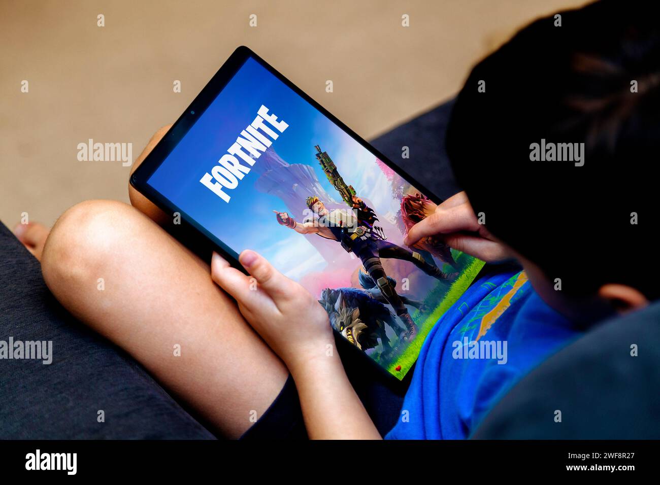 Fortnite game app on tablet screen in kid's hands close-up. Little boy ...