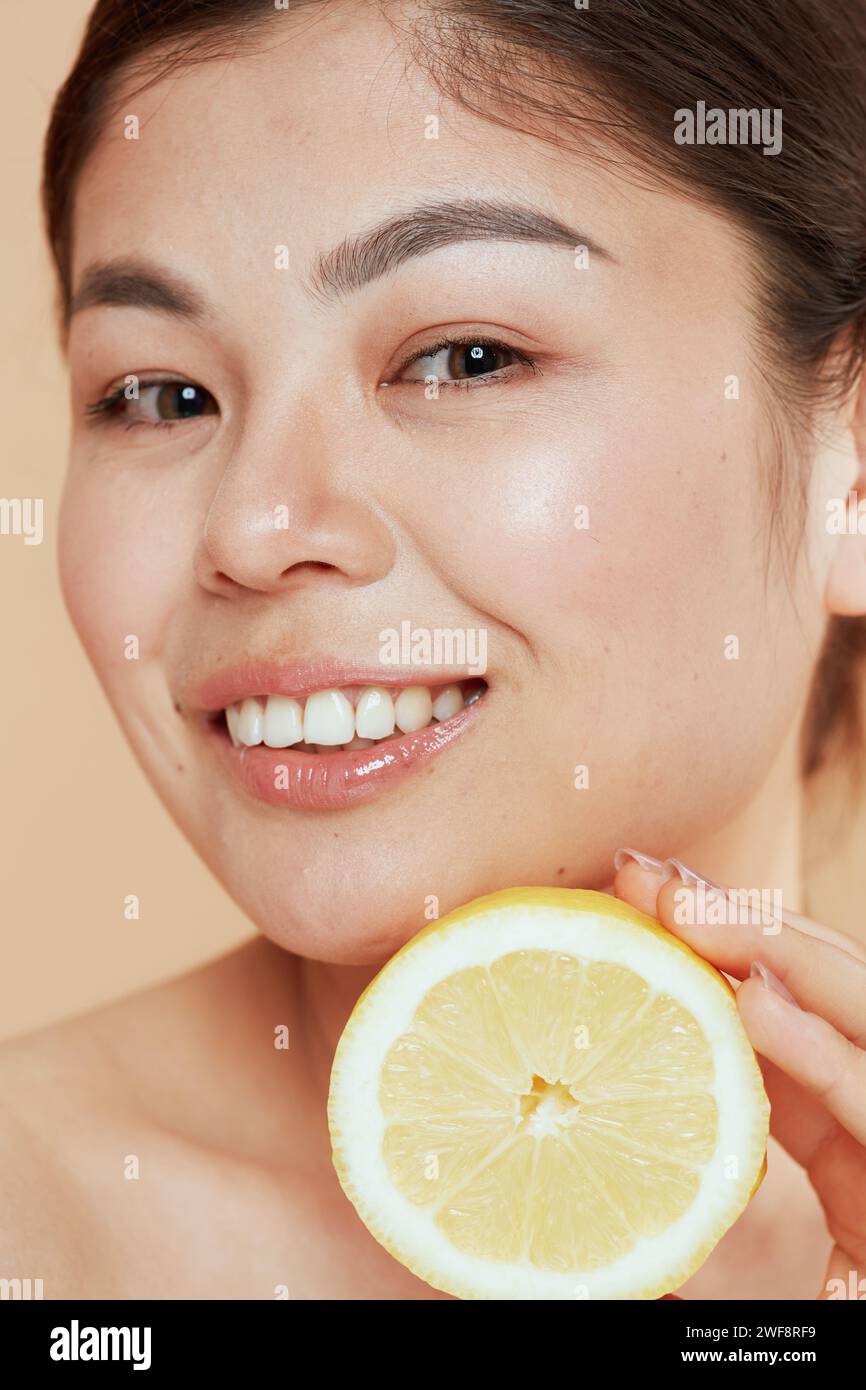 Portrait of modern asian female with lemon against beige background ...