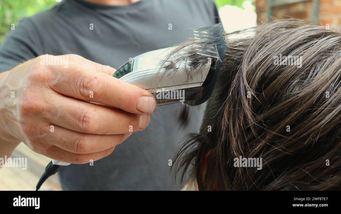 male hand of a hairdresser holds a hair machine near the head of a long ...